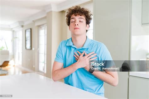 얼굴에 눈을 감고 감사 제스처와 가슴에 손으로 웃 고 집에서 캐주얼 블루 티셔츠를 입고 젊은 잘생긴 남자 건강 개념입니다 T 셔츠에 대한 스톡 사진 및 기타 이미지 Istock