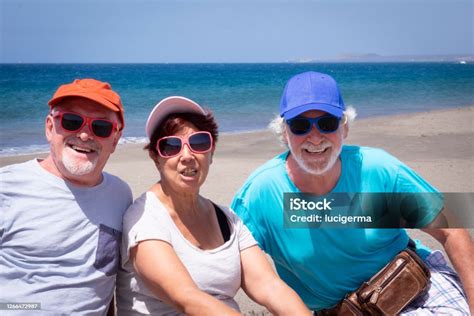 해변에 앉아 세 친구의 쾌활한 그룹 태양과 여름을 즐기는 바다 미소에서 야외 휴가에서 은퇴 한 성인 사람들 수염 남자 물 위에 수평선 3 명에 대한 스톡 사진 및 기타