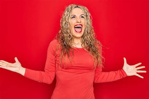 고립 된 배경에 서 빨간색 캐주얼 티셔츠를 입고 젊은 아름다운 금발 의 여자 미친 미친 소리와 공격적인 표정과 팔을 제기 고함 좌절 개념입니다 T 셔츠에 대한 스톡 사진 및