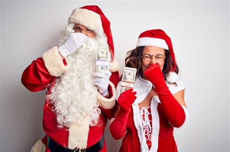 산타 클로스 의상을 입고 선임 부부는 코에 손가락으로 숨을 들고 냄새와 역겨운 참을 수없는 냄새를 맡고 고립 된 흰색 배경 위에 달러를 들고 나쁜 냄새 개념 2명에 대한