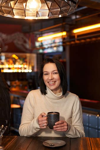 우아한 특징과 어두운 어깨 길이의 머리를 가진 아름다운 소녀는 카페에 앉아 웃고 그녀의 손에 머그잔을 들고 30 34세에 대한 스톡 사진 및 기타 이미지 Istock