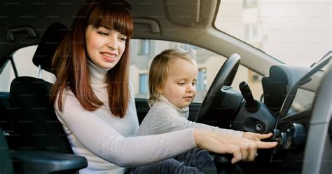 귀여운 어린 소녀 아이가 차에서 놀고 음악이나 라디오를 듣고 자동차 핸들 근처의 앞 좌석에 함께 앉아 있는 젊은 어머니 가족 여행 차에 아이 사진