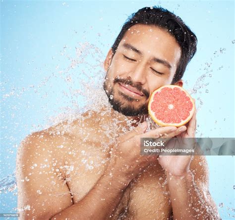 얼굴 물 자몽은 위생이나 자연 수분 공급을 위해 파란색 배경에 스튜디오에 있는 남자 모델입니다 스킨 케어 아름다움 또는 과일 잘 생긴 젊은 남성이 샤워 할 때 물 튀김에서