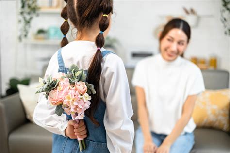 소파에 앉아있는 매력적인 아름다운 아시아 엄마 딸은 가족의 순간에 선물 상자와 꽃을줍니다 소파에 앉아있는 여성 또는 어머니의 날 또는 생일 25 29세에 대한 스톡 사진 및