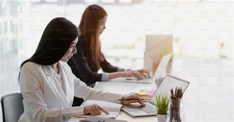 사무실의 흰색 테이블에 사무용품과 장식으로 노트북에 타이핑하는 두 사업가의 측면 모습 사진 Unsplash의 앉아 이미지