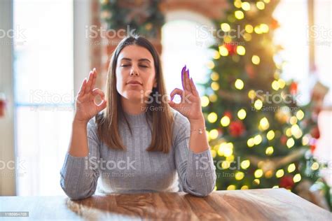 크리스마스 트리와 장식 주위에 집에서 테이블에 앉아 젊은 아름다운 여성은 손가락으로 명상 제스처를하고 눈을 감고 미소 요가 개념입니다 크리스마스에 대한 스톡 사진 및 기타