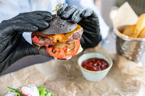 감자 튀김과 신선한 맛있는 햄버거를 들고 검은 장갑에 여성의 손 샐러드와 감자 튀김 패스트 푸드를 먹는 여자와 카페에서 햄버거