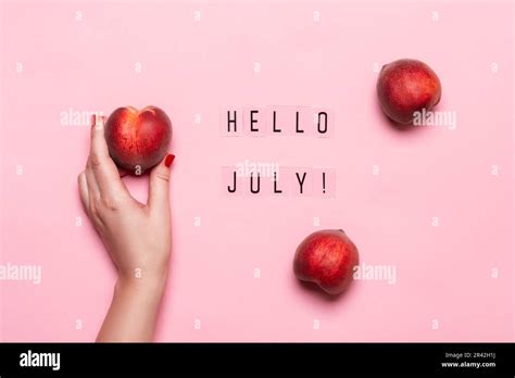 Hello July Text And Female Hand Holds Ripe Peach On Pink Background