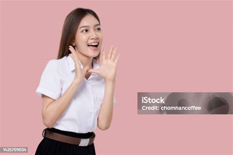 대학 유니폼을 입은 아시아 민족의 십대 학생 소녀가 입을 벌리고 분홍색 배경에 고립 된 비명을 지르는 발표를 들고 있습니다 학생에 대한 스톡 사진 및 기타 이미지 Istock