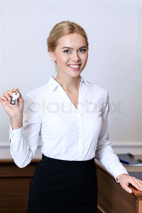 Smiling Attractive Receptionist Holding Key At Reception Desk Stock