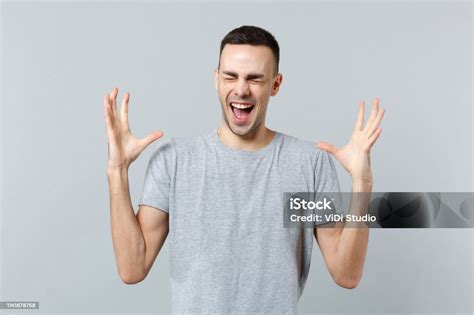 미친 남자의 초상화는 스튜디오에서 회색 벽 배경에 고립 된 손을 확산 눈을 유지 캐주얼 옷을 비명 사람들은 진심으로 감정 라이프 스타일 개념입니다 복사 공간을 모의 합니다