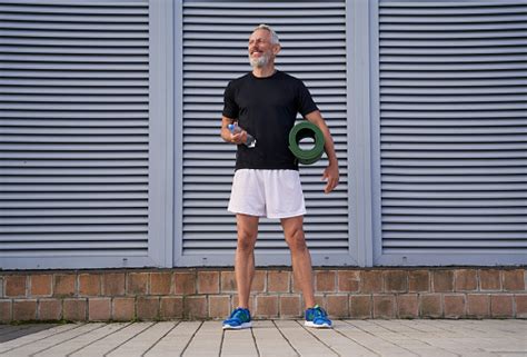 쾌활한 중년 스포츠맨이 옆으로 웃고 운동 매트와 물 한 병을 들고 야외에서 스포츠를 할 준비가 되었습니다 45 49세에 대한 스톡 사진 및 기타 이미지 Istock