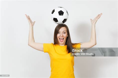 아름 다운 유럽 젊은 명랑 한 여자 축구 팬 또는 플레이어 머리 축구공 위에 들고 노란색 유니폼에 흰색 배경에 고립 스포츠 축구