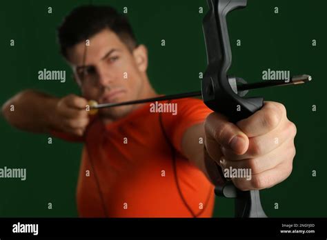 Man With Bow And Arrow Practicing Archery Against Green Background Focus On Hand Stock Photo