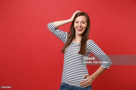 서 밝은 빨간 벽 배경에 고립의 머리에 손을 줄무늬 옷에 즐거운 매력적인 젊은 여자의 초상화 사람들이 진심으 감정 라이프 스타일 개념 복사 공간을 비웃는 다 갈색 머리에
