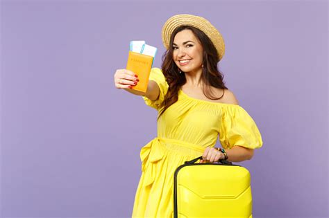 노란 드레스 여름 모자 개최 여행 가방 여권 탑승권 티켓 파스텔 바이올렛 벽 배경에 고립에서 아름 다운 젊은 여자 사람들은 진심으로 감정 라이프 스타일 개념입니다 복사