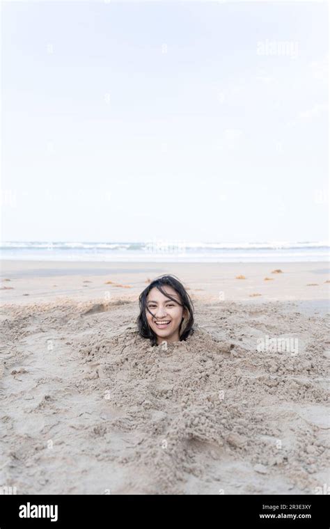 A Young Hispanic Woman Is Having Fun While Buried In The Sand Of The