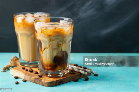 크림을 뿌린 높은 유리에 아이스 커피를 쏟아붓고 가벼운 돌 배경에 커피 콩을 뿌립니다 튜브가있는 추운 여름 음료 복사 공간 0