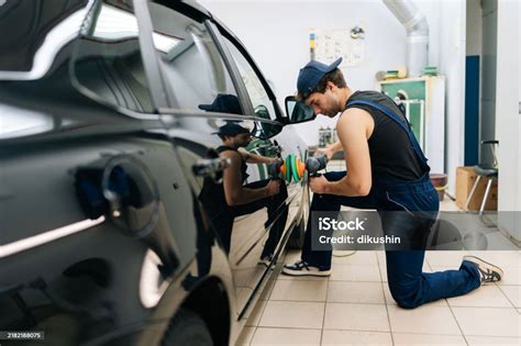 궤도 광택기와 함께 사용하는 자동차 수리점에서 고급 자동차의 문을 닦는 모자에 집중된 정비사 노동자 남성 자동차 연마기를 사용하는 전문 자동차 페인트 기술자 자동차 수리