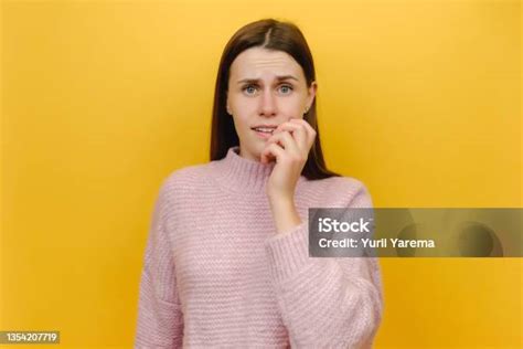 고민 사려 깊은 펜서디의 초상화 무서운 오해젊은 여자 물린 손톱 손가락을 물어 카메라 핑크 니트 스웨터를 입고 노란색 색상 배경 스튜디오를 통해 고립 포즈 겁먹은에 대한