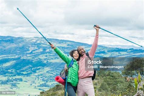 흑인 남자와 아프리카 여자는 손을 들고 있는 트레킹 폴을 껴안고 들어 올리면서 산 꼭대기에서 즐기고 웃습니다 2명에 대한 스톡 사진 및 기타 이미지 Istock