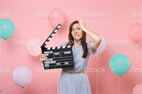 다채로운 공기 Baloons와 분홍색 배경에 Clapperboard 만드는 고전적인 흑인 영화를 들고 머리에 기대 며 입술을 물어 뜯고 하는 파란 드레스에 불만족된 우려