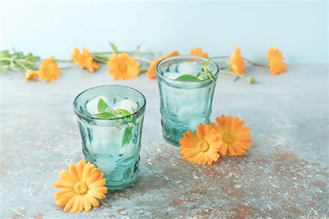 차가운 음료와 얼음 큐브가있는 두 개의 아름다운 빈티지 청록색 안경 천연 다채로운 석조 테이블에 메리 골드 꽃으로 장식 된