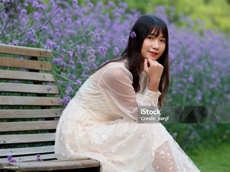 보라색 버베나 보나리엔시스 꽃밭 사이에 벤치에 앉아 있는 흰색 드레스를 입은 아름다운 여성 검은 긴 머리를 가진 매력적인 중국 소녀는 야외에서 여가 시간을 즐깁니다 20
