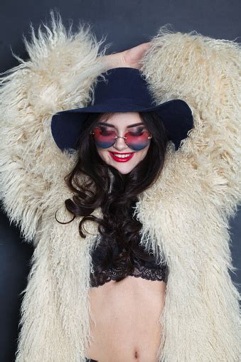 밝은 메이크업과 긴 웨이브 머리를 가진 행복 한 젊은 성인 여성 패션 모델 파란색 모자와 선글라스를 착용 푸른 스튜디오 벽 배경에 포즈를 취하고 있습니다 18 19세에 대한