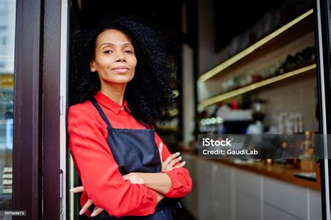빵집 입구에 서있는 동안 크로스 손으로 바리스타를 작업하는 자신감 있는 아프리카 계 미국인 젊은 여성의 절반 길이 초상화 카페 개발 소매 업의 경험이 풍부한 어두운 피부