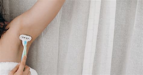 플라스틱 면도기를 들고 털이 많은 겨드랑이를 면도하는 손 젊은 여자는 집 욕실에서 플라스틱 면도기 근접 촬영으로 겨드랑이를 면도합니다 피부 관리 제모 개념 복사 공간