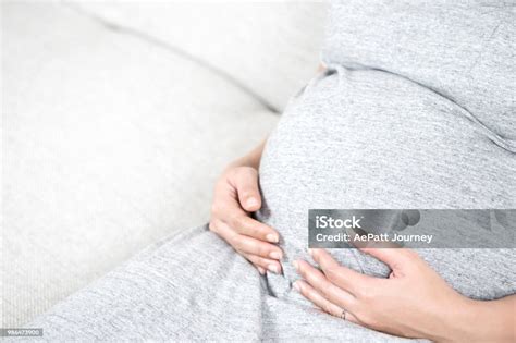 젊은 아름 다운 임신한 여자 집에서 회색 소파와 그녀의 배꼽에 감동 하는 보유 손에 앉아 가족에 대한 스톡 사진 및 기타 이미지 가족 개념 기대 Istock