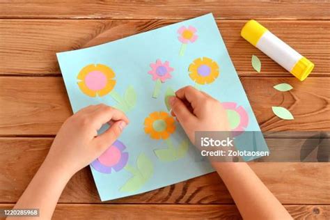 꽃이 있는 카드를 하는 아이 한 어린이가 종이 잎을 손에 들고 붙입니다 카드 만들기를위한 종이 꽃 접착제 나무 테이블에 인사말 카드 아이에 대한 스톡 사진 및 기타 이미지