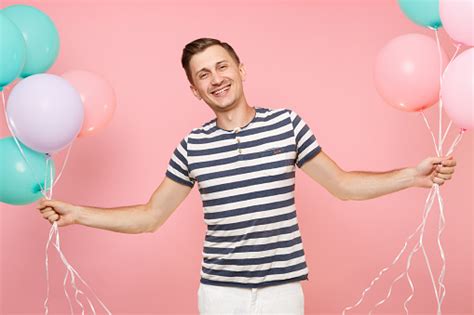 밝은 동향 분홍색 배경에 고립 된 다채로운 공기 풍선 들고 줄무늬 티셔츠를 입고 매혹적인 젊은 행복 한 남자의 초상화 사람들이 진심으 감정 라이프 스타일 개념 광고