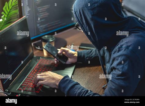 Man Hacker In The Hood Is Programming Virus Code At The Keyboard For The Laptop The Concept Of