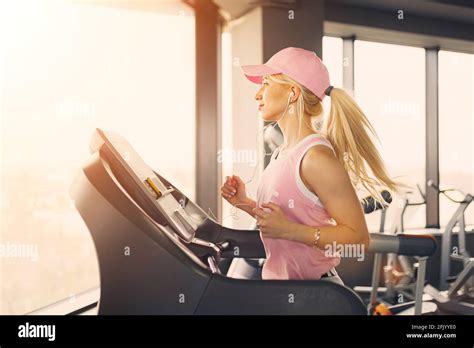 Side View Of Sporty Blonde Woman Exercising On Treadmill In Gym Stock