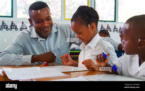 A Teacher Engages With Two Students Working On Their Assignments Stock