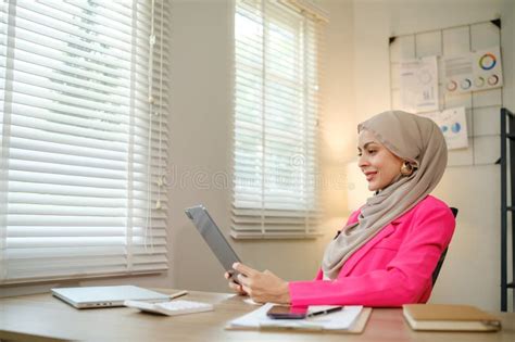 A Woman Wearing A Pink Jacket Is Sitting At A Desk With A Tablet In