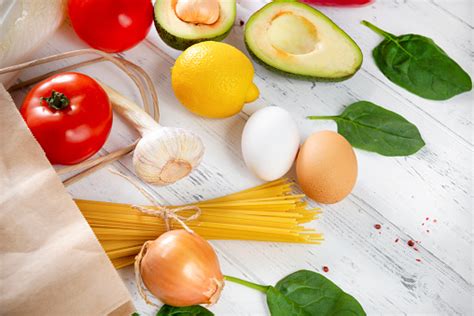 신선한 야채와 과일은 흰색 나무 배경에 종이 식료품 가방에서 유출 토마토 아보카도 고추 양상추 레몬 파스타 계란 마늘 양파 시금치 해독 소박한 바이오 가방에 대한 스톡 사진