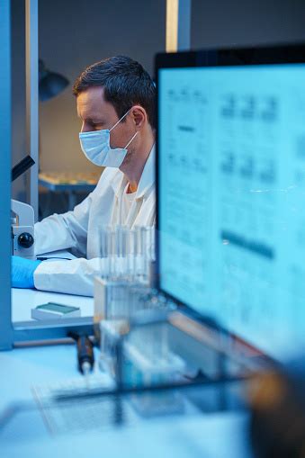 흰색 실험실 코트 보호 마스크 및 장갑을 착용 한 과학자가 현대 실험실에서 현미경으로 작업하는 우리는 전경에 컴퓨터 모니터를 봅니다 핀란드에 대한 스톡 사진 및 기타 이미지