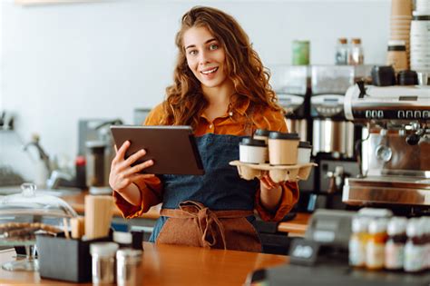 곱슬 머리와 태블릿을 손에 들고 커피 숍의 잘 생긴 젊은 매니저는 커피 숍에서 테이크 아웃 커피를 제공합니다 테이크 아웃 음식 사업 개념입니다 20 24세에 대한 스톡 사진