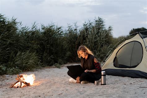 해변에서 저녁 텐트 캠핑 여성 여행자는 모닥불 옆에 앉아 노트북 컴퓨터를 사용합니다 원격 근무 전자 쇼핑 전자 상거래 인터넷