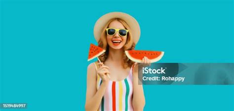 신선한 육즙이 많은 과일 막대 사탕 또는 아이스크림 모양의 수박 조각이 파란색 배경에 밀짚모자를 쓰고 있는 행복한 미소 짓는 젊은 여성의 여름 초상화 25 29세에 대한