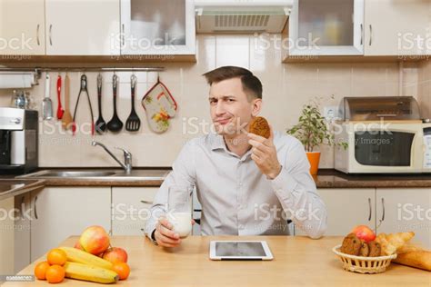 아침 식사 태블릿 귀리 쿠키와 함께 앉아 가벼운 부엌에 우유와 시리얼을 먹는 격자 무늬 셔츠에 잘생긴 백인 젊은 비즈니스 사람 건강 한 생활양식입니다 집에서 요리 음식 준비