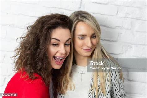 두 젊은 성인 백인 여자 친구 재미와 실내 흰색 벽돌 벽에 대 한 함께 시간을 보내고 즐길 수 있습니다 집에서 소셜 네트워크에 대한 사진을 만드는 속임수와 바보 친구의 쌍