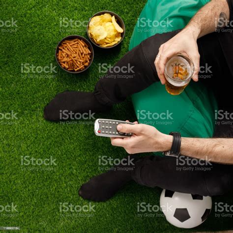 한 남자가 Tv에 앉아 축구 경기를 관람하고 있다 스네키 Tv 리모컨 축구 공입니다 위에서 볼 수 있습니다 공간을 복사합니다 잔디의 모방 Championship에 대한 스톡