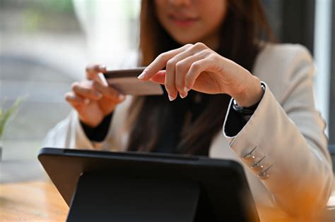 양손으로 신용 카드를 들고 사무실에 앉아 금융 및 기술 개념을 위해 태블릿에서 일하는 양복을 입은 웃는 아시아 여성의 모습이 잘린 모습 30 34세에 대한 스톡 사진 및