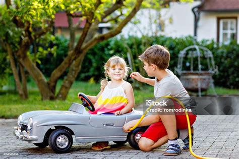 야외에서 여름 정원에서 큰 오래 된 장난감 자동차를 가지고 노는 두 명의 행복한 아이들 꼬마 소년은 어린 유아 소녀와 함께 자동차에 연료를 보급합니다 2명에 대한 스톡 사진