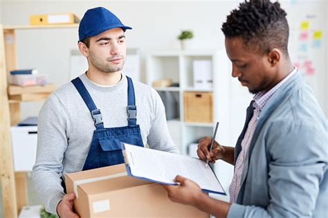 심각한 진정 젊은 장 수 모자 관리자 문서에 배달에 대 한 서명 검은 사무실 동안 골 판지 상자를 들고 남자에 대한 스톡 사진 및 기타 이미지 Istock