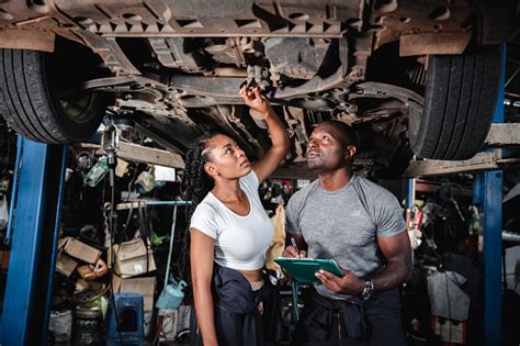 두 명의 정비사가 차고에서 자동차 아래 부품을 검사하고 체크리스트합니다 수리 자동차 서비스 개념 기계공에 대한 스톡 사진 및
